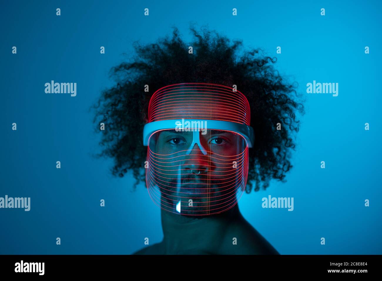Serious young man wearing red led mask against wall at home Stock Photo ...