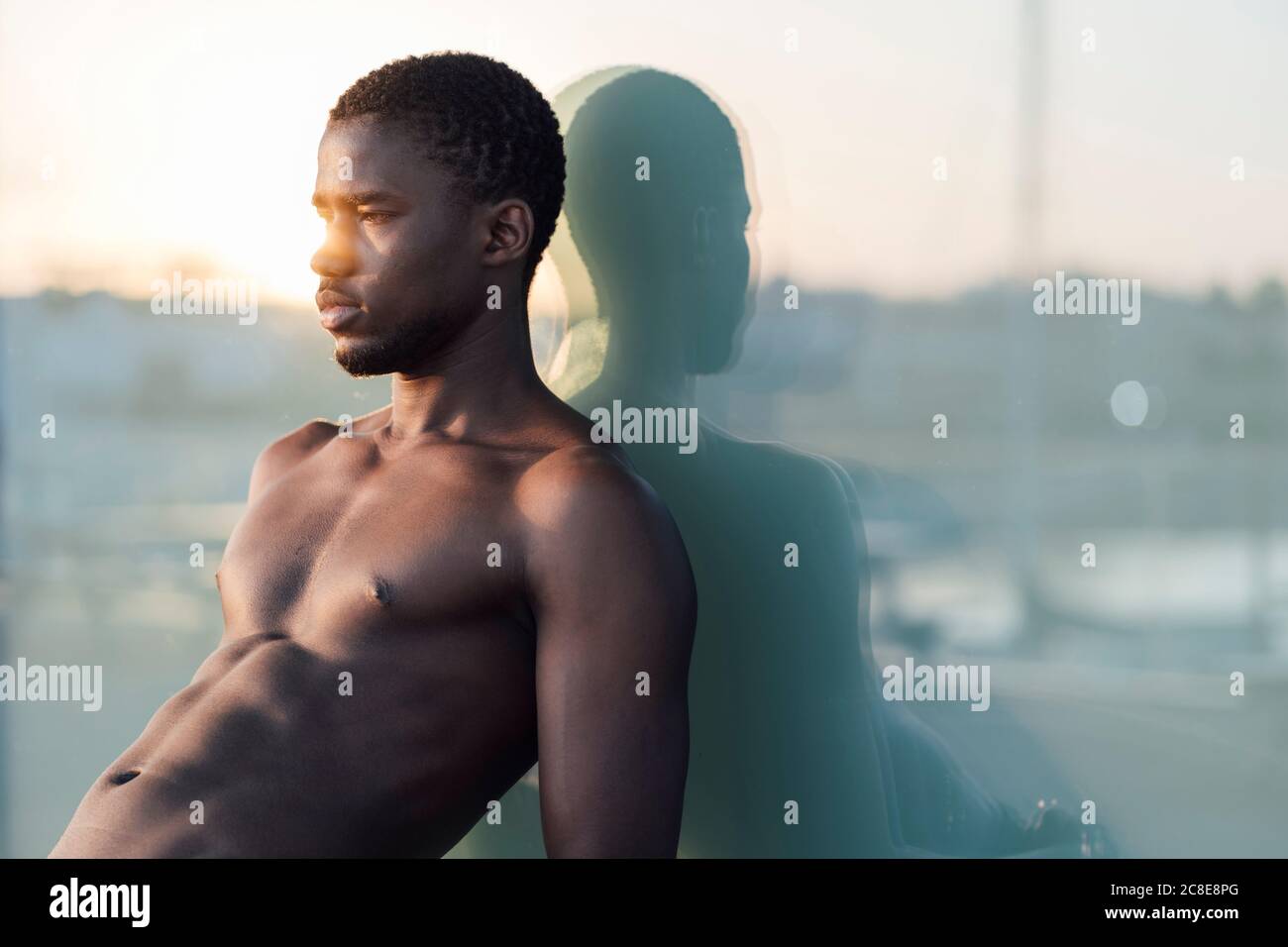 Young shirtless man leaning on window glass Stock Photo - Alamy