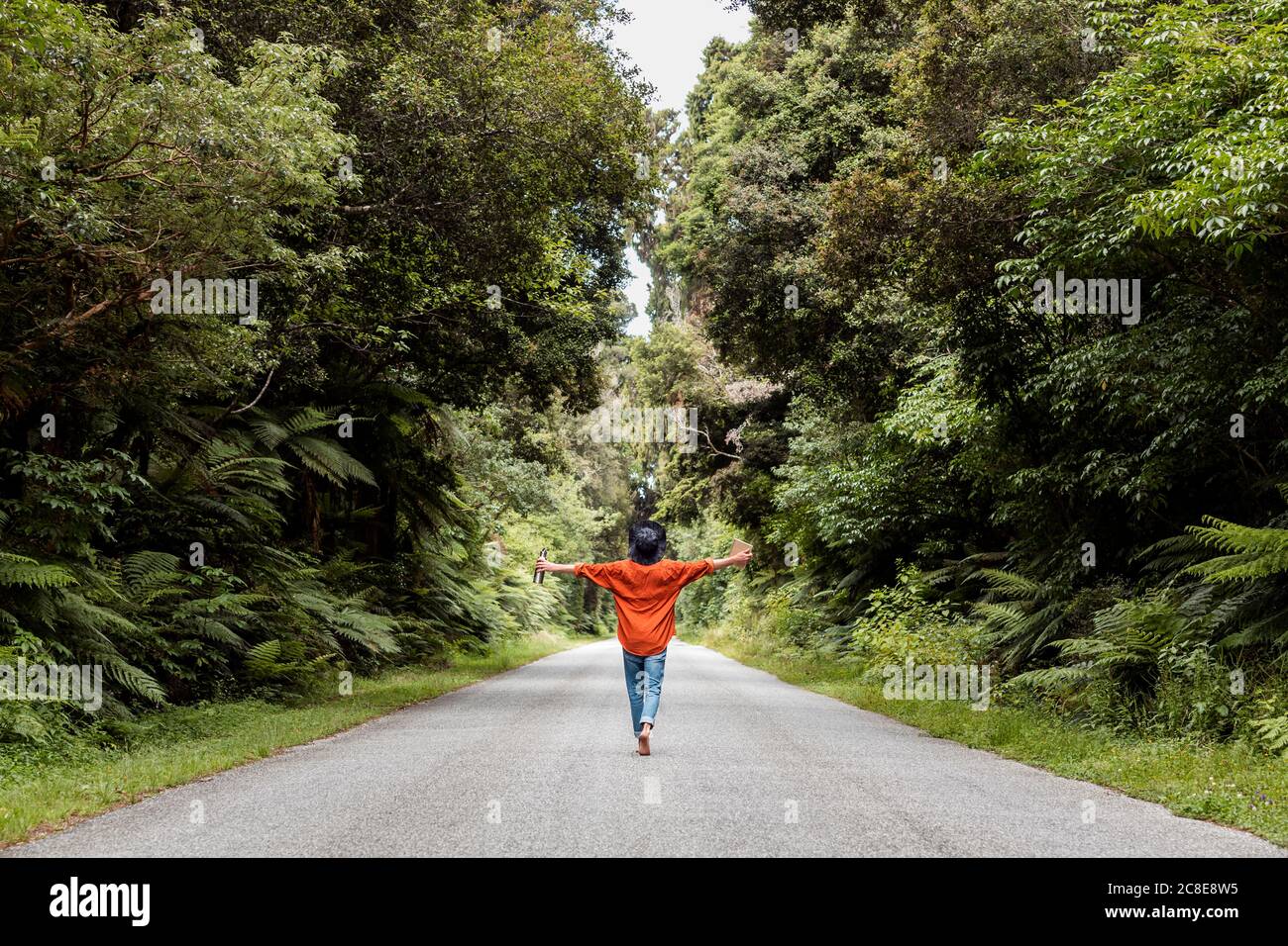 Young man walking with arms outstretched on country road in forest ...