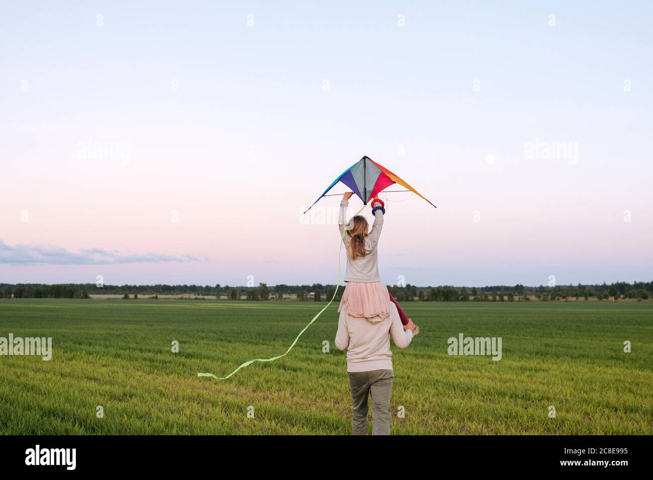 Man carrying daughter holding kite on shoulders while walking on grassy ...