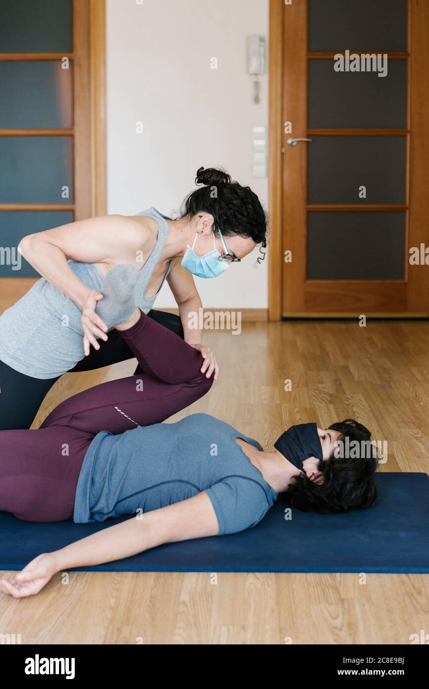Physiotherapist wearing mask stretching female patient's leg lying on ...