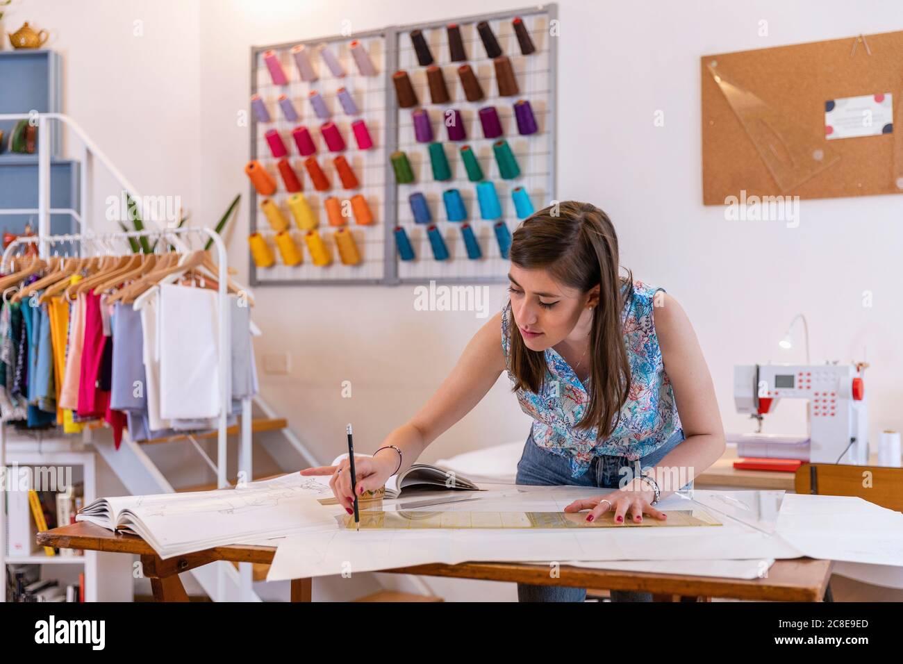 Beautiful young female designing trainee drawing on paper at workbench ...