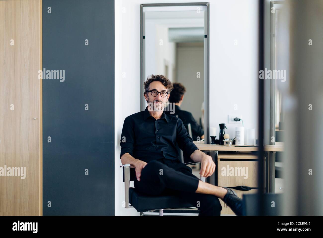 Confident male hairdresser sitting on chair in salon Stock Photo - Alamy