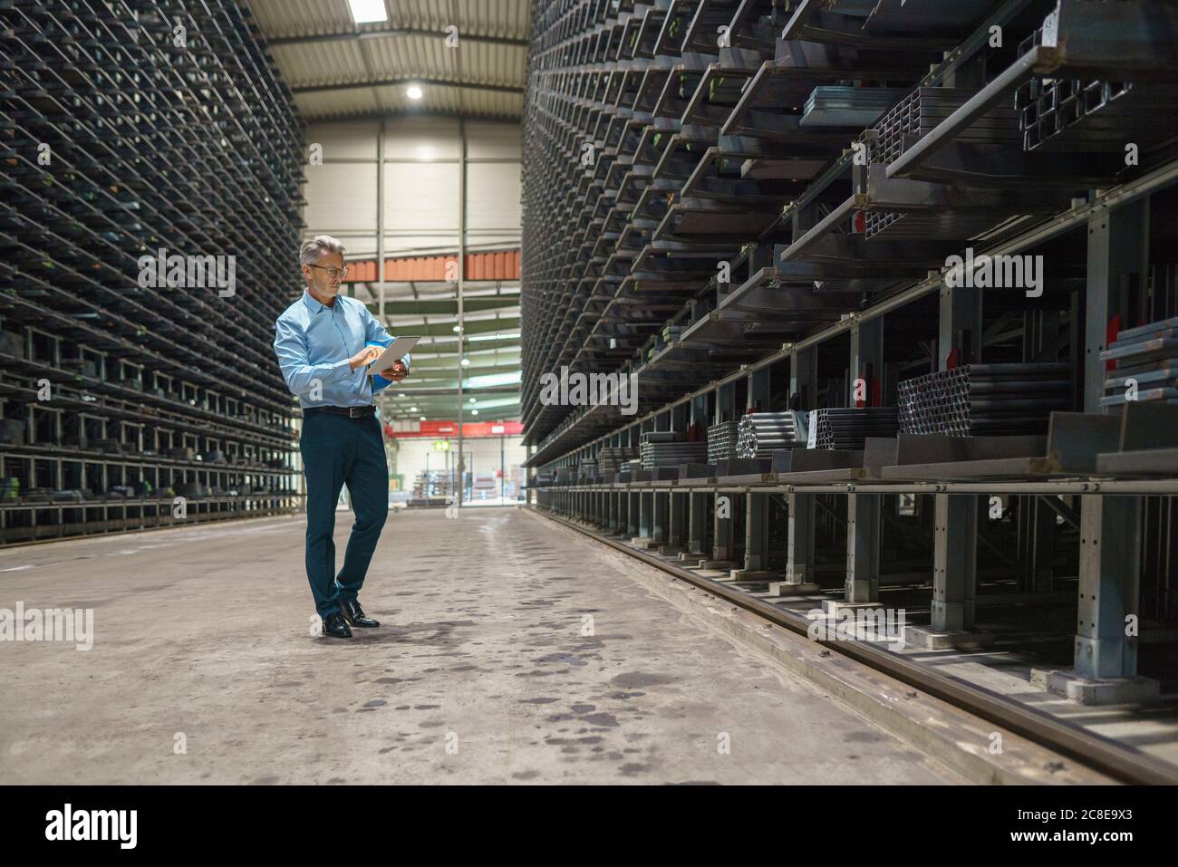 Mature businessman using tablet in a high rack warehouse of a factory ...