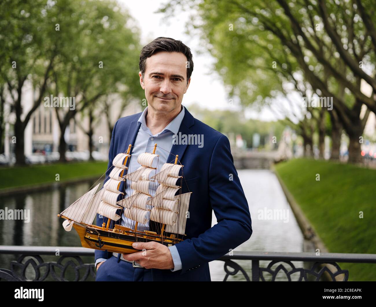 Portrait of a confident mature businessman holding model sailing ship ...