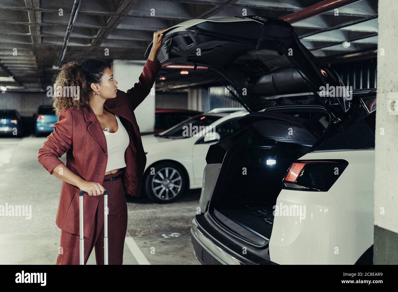 Young female professional on business trip closing car trunk at parking ...