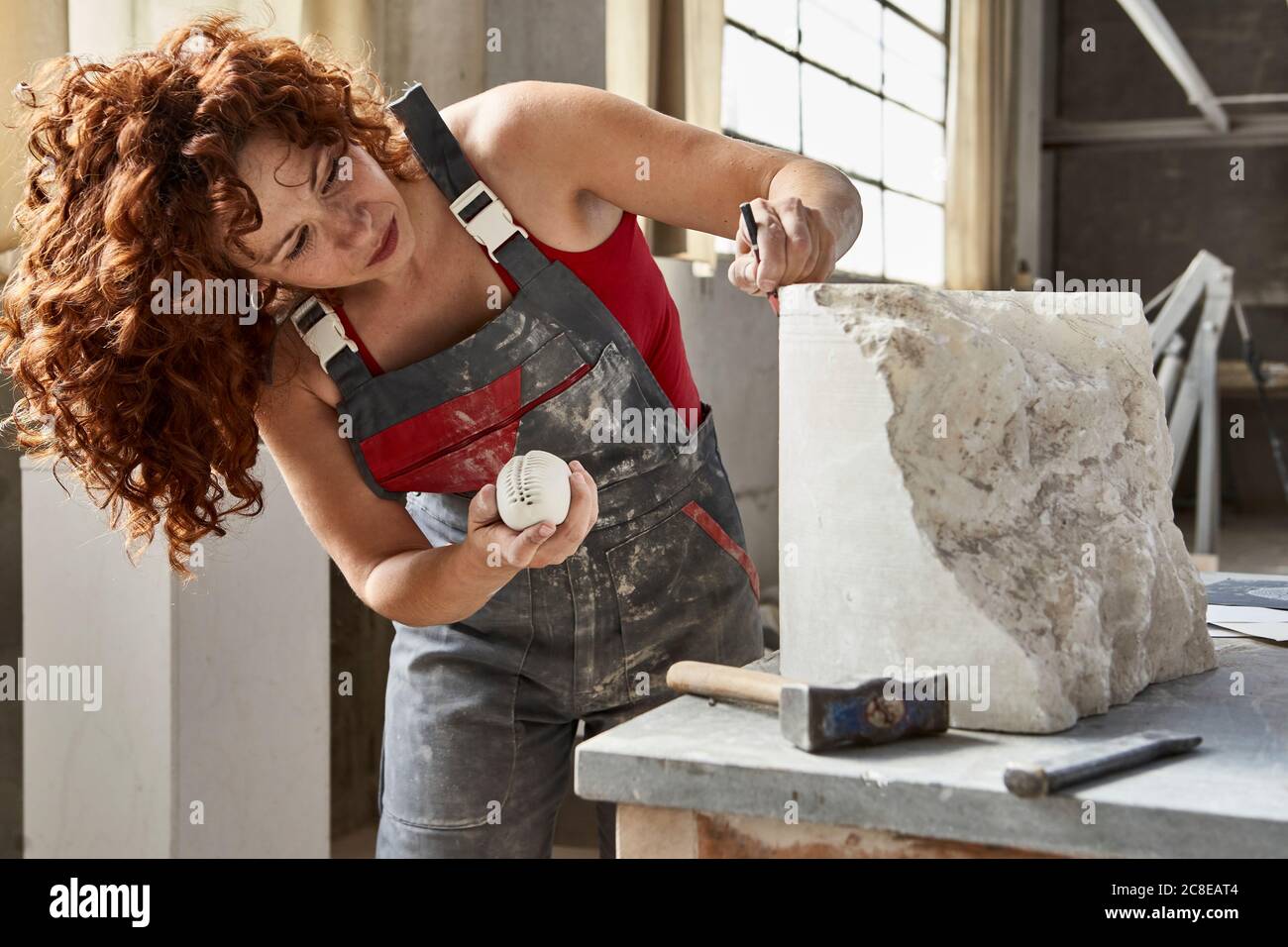 Female stonemason in overalls measuring stone on table at workshop ...