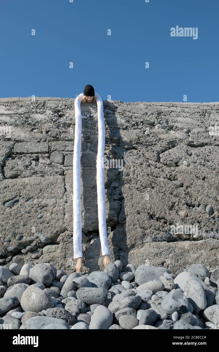 Woman with artificial long hands bending over retaining wall at beach ...
