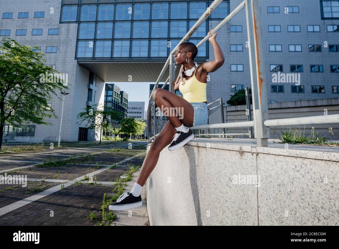 Thoughtful young woman sitting on railing against building in city ...