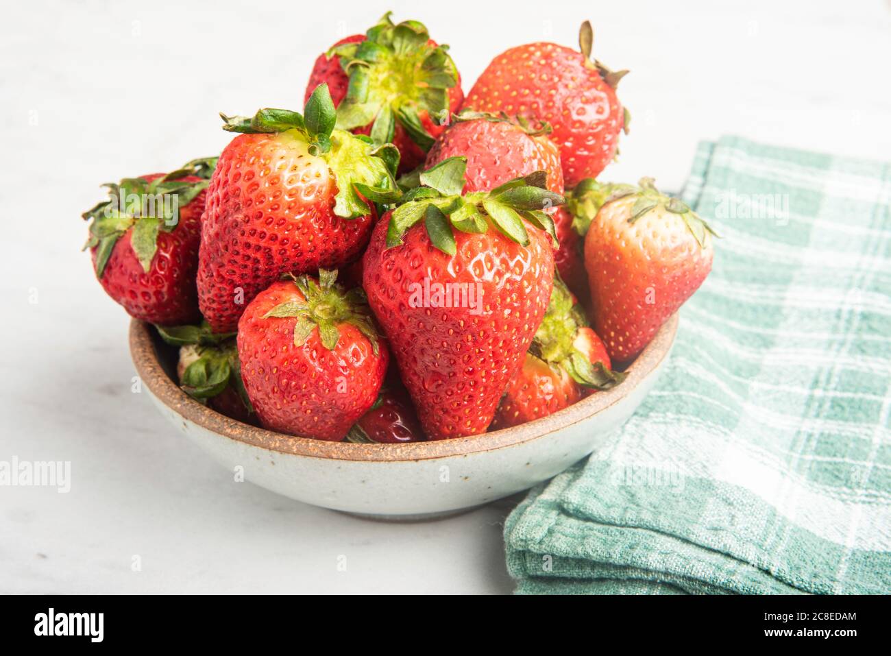 A ceramic bowl of fresh and sweet red strawberries set on a marble ...