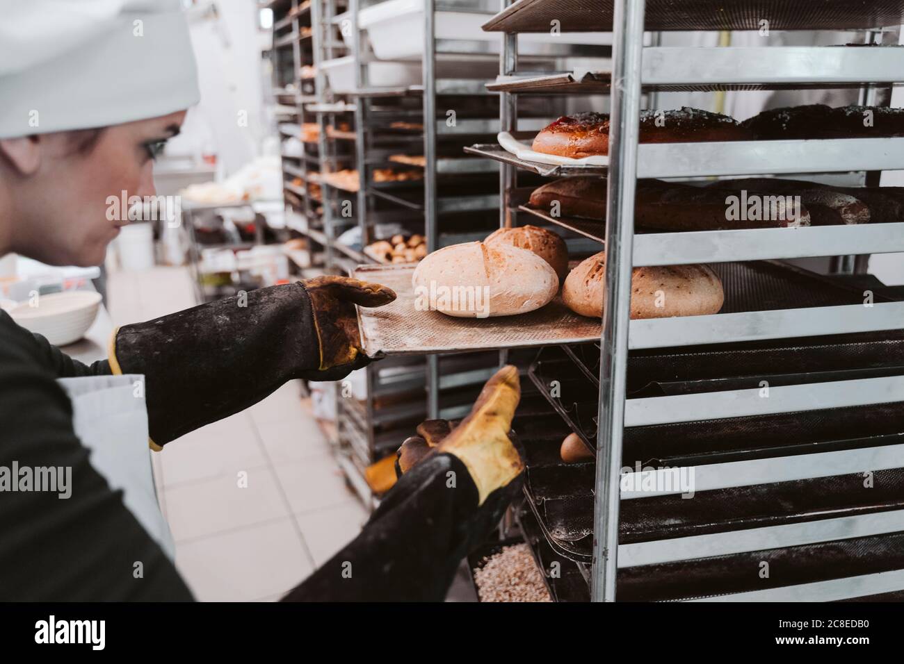 Female baker inserting bun tray in trolley at bakery Stock Photo - Alamy