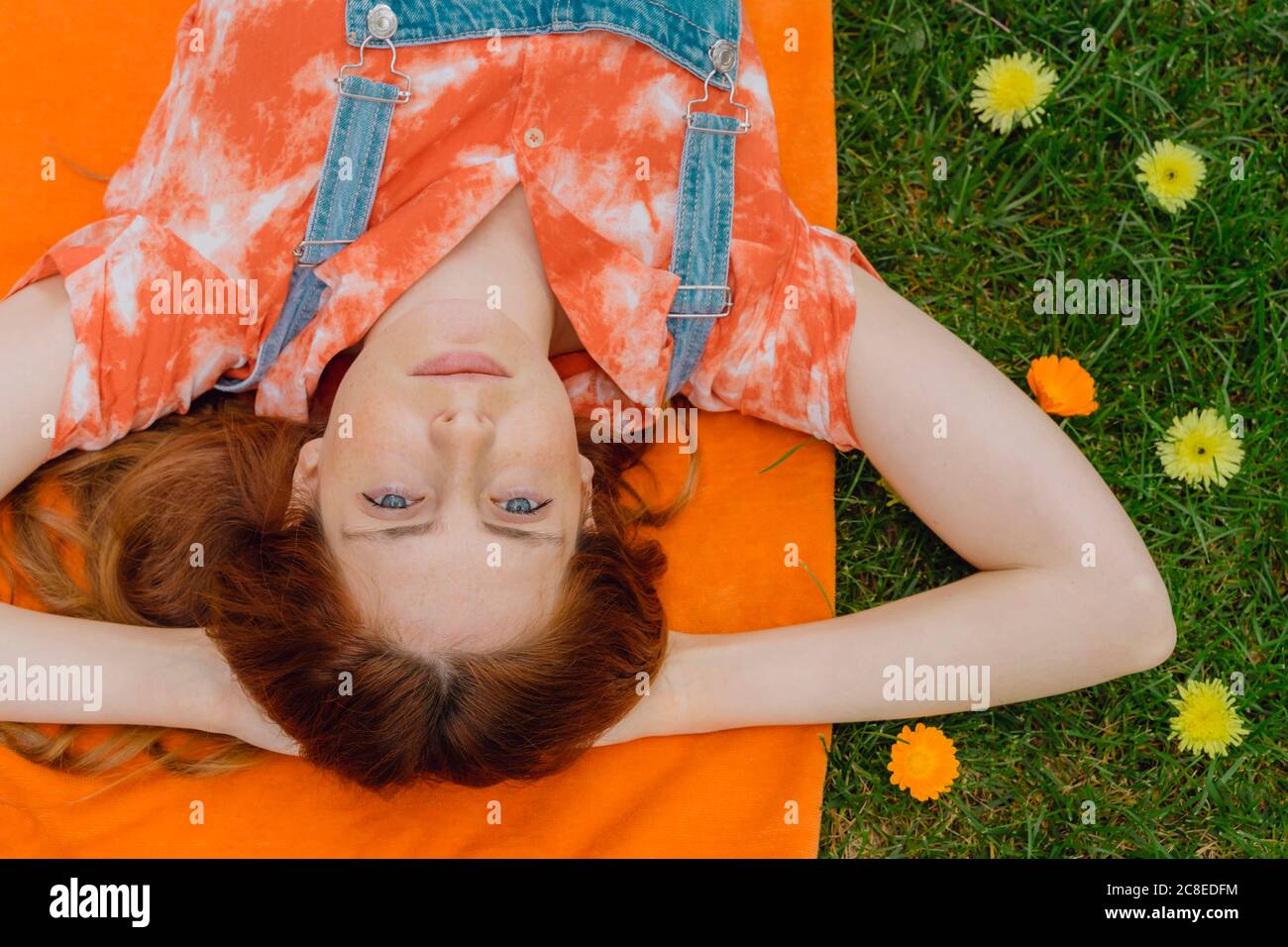 Relaxed Young Woman Lying With Hands Behind Head On Picnic Blanket By