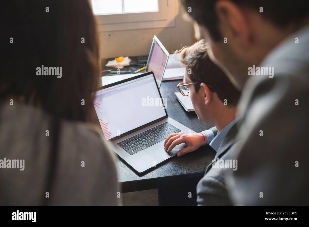 Three business people sharing laptop at desk in office Stock Photo - Alamy