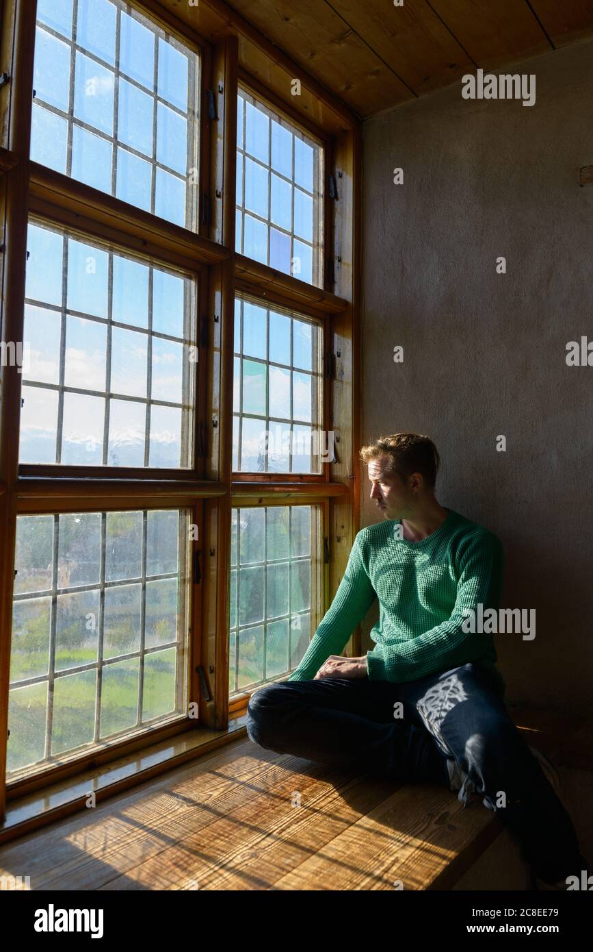 Young handsome man sitting in front of closed wooden window with ...