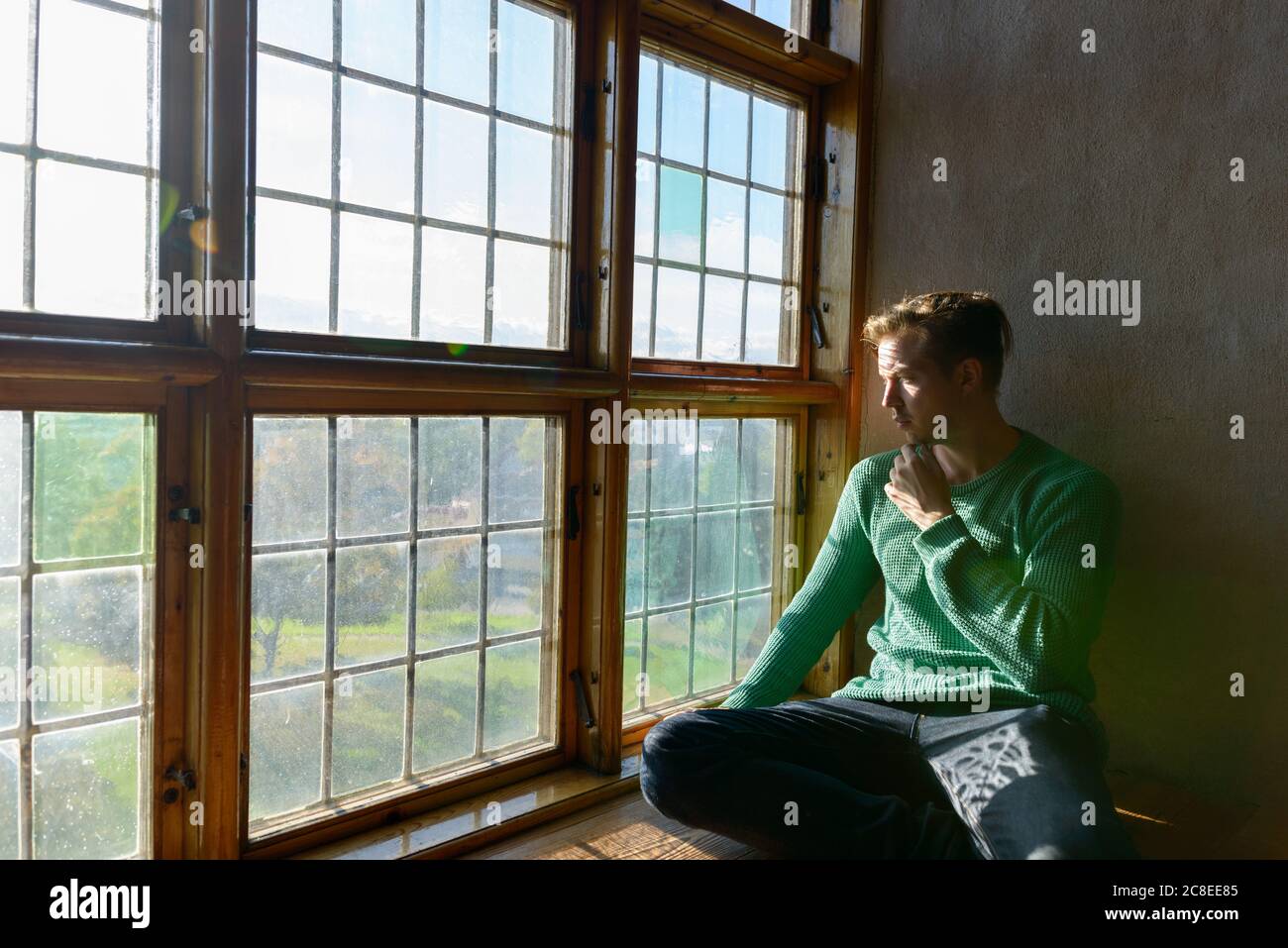 Young handsome man thinking in front of closed wooden window with ...