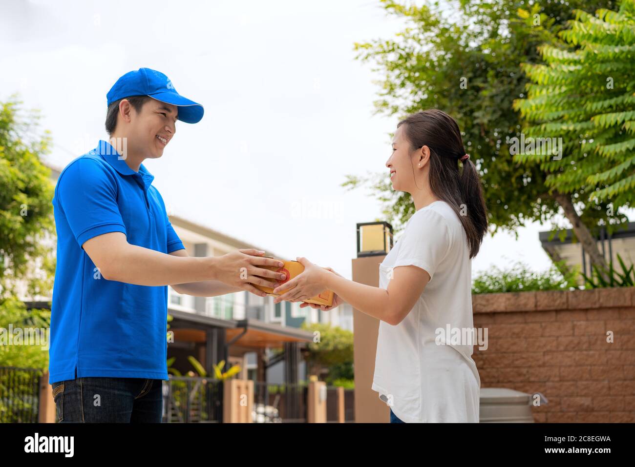 Asian delivery young man in blue uniform smile and holding a cardboard ...