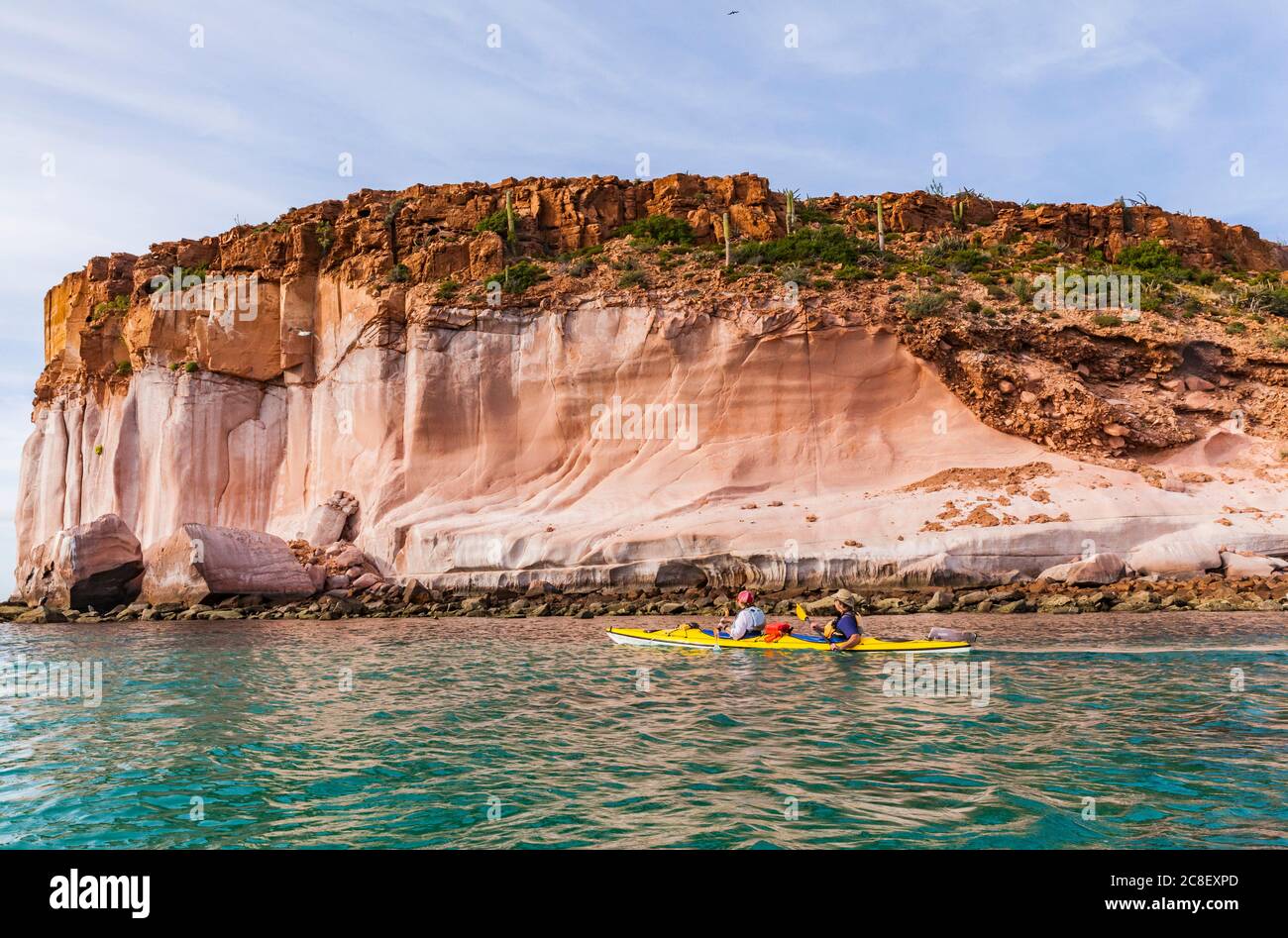 A couple sea kayaking offshore below towering sandstone cliffs on Isla ...