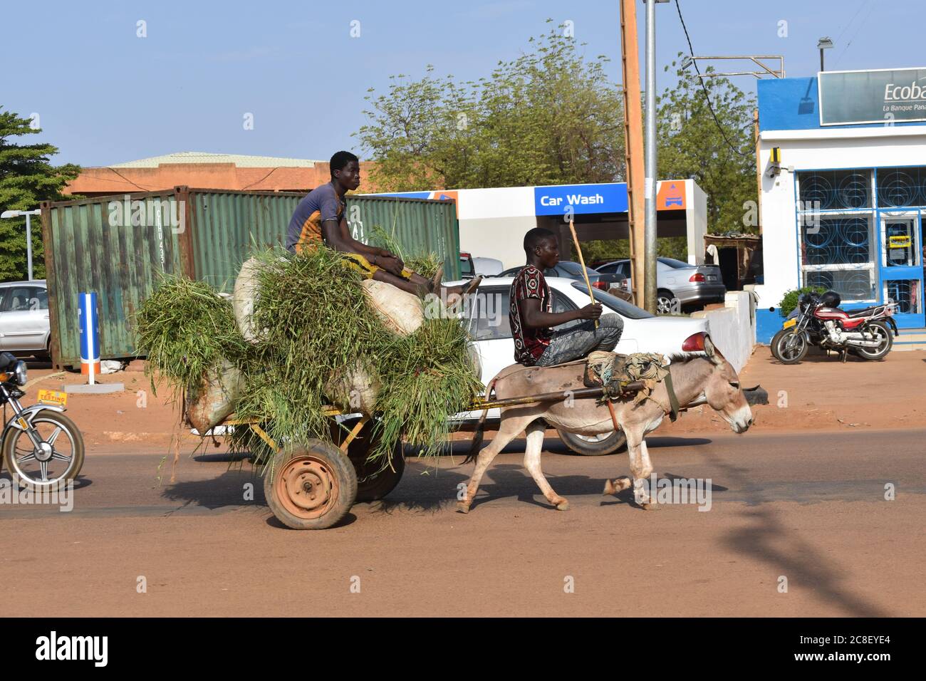 A donkey pulling a loaded cart of hay down an African street (with two ...