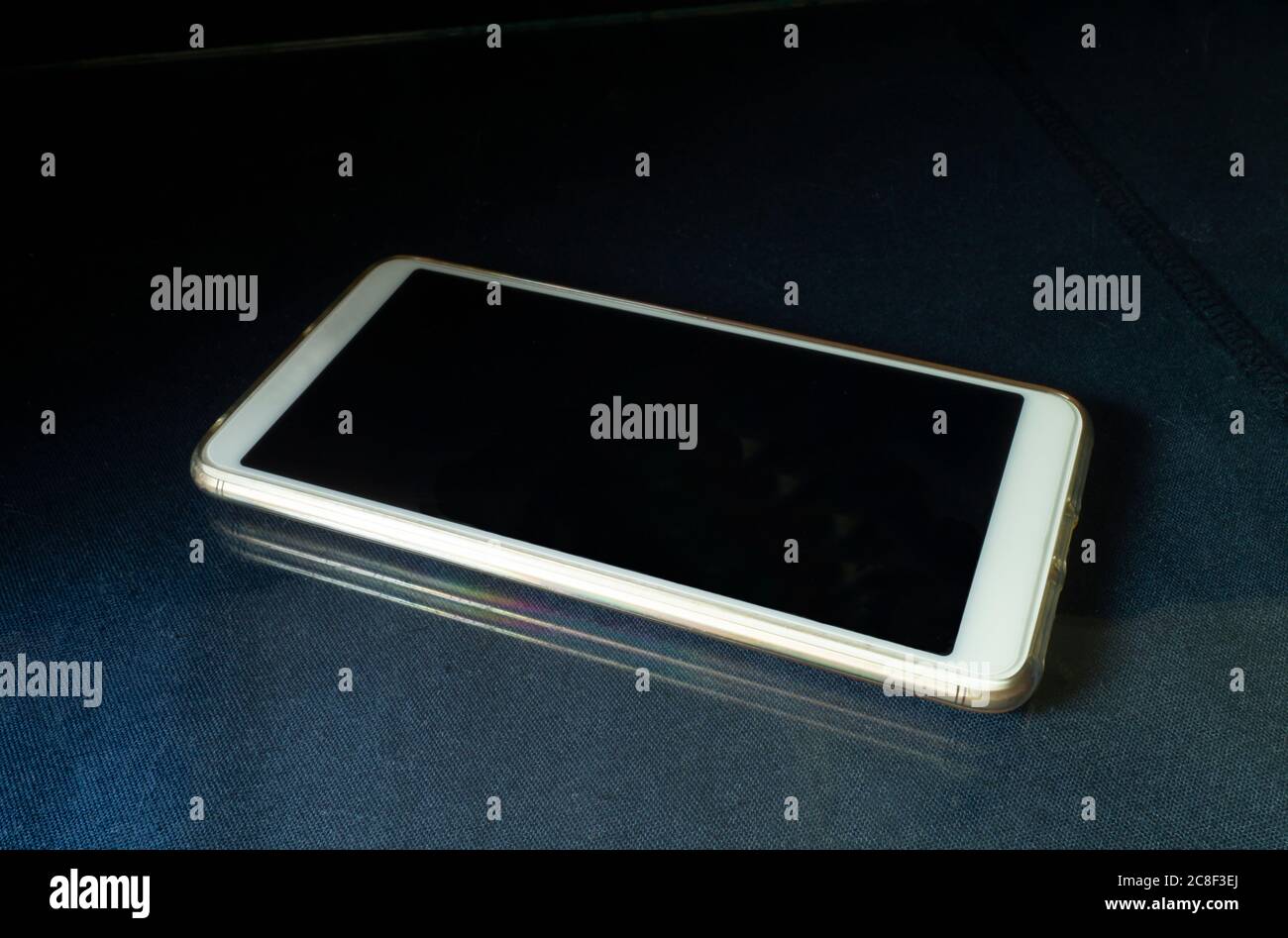 Mobile telephone of the white colour on black background rests upon ...