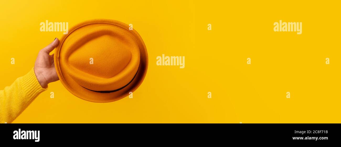 fashionable yellow felt hat in hand over yellow background, panoramic ...