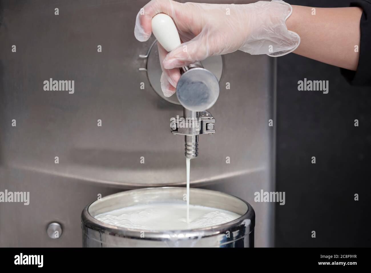 Close-up of the hand of a worker who fills fresh milk from a milk tank ...