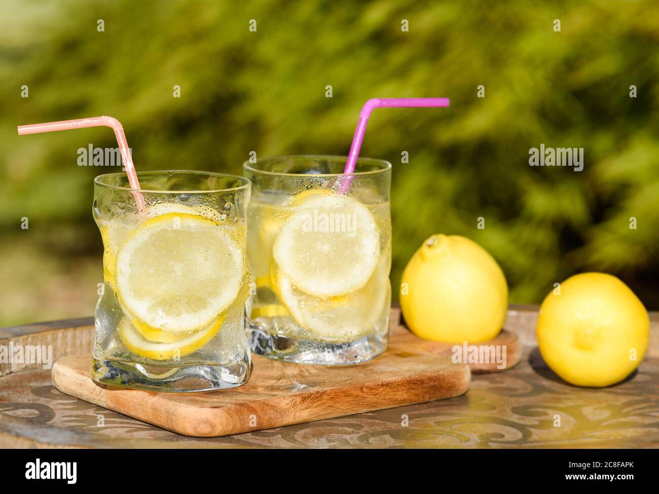 Lemonade in glass with slices of lemon and straws in the garden on ...
