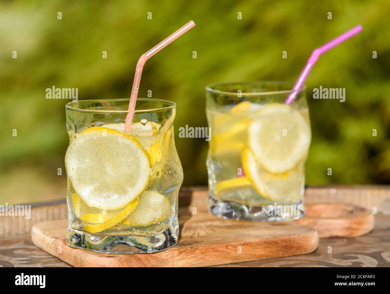Lemonade in glass with slices of lemon and straws in the garden on ...