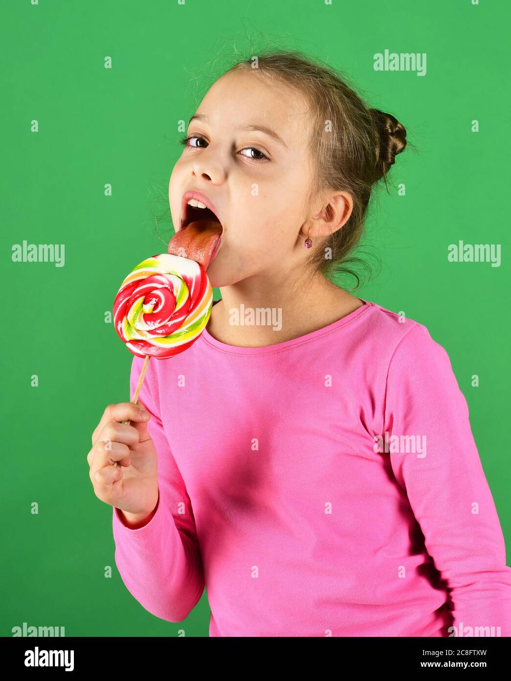 Child with happy face poses with candy on green background. Girl eats ...