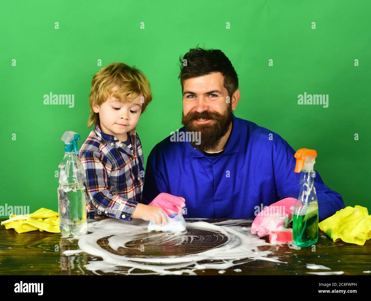 Dad with son and cleaning supplies on green background. Father with ...