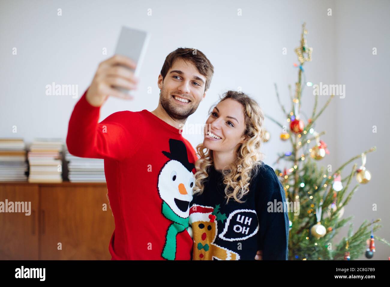 Couple taking selfie in front of Christmas tree at home Stock Photo - Alamy