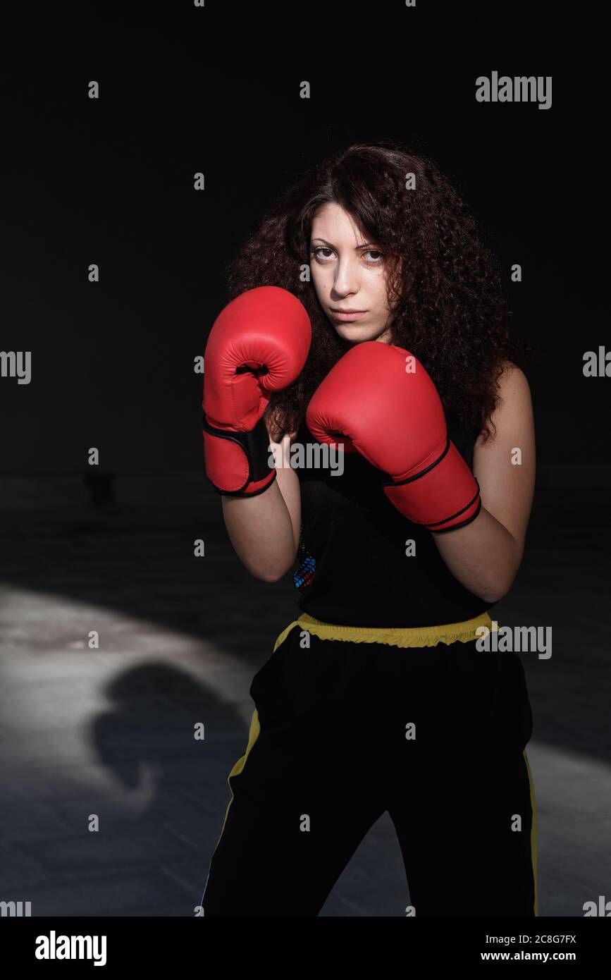 Portrait of young woman with long brown hair wearing red boxing gloves ...
