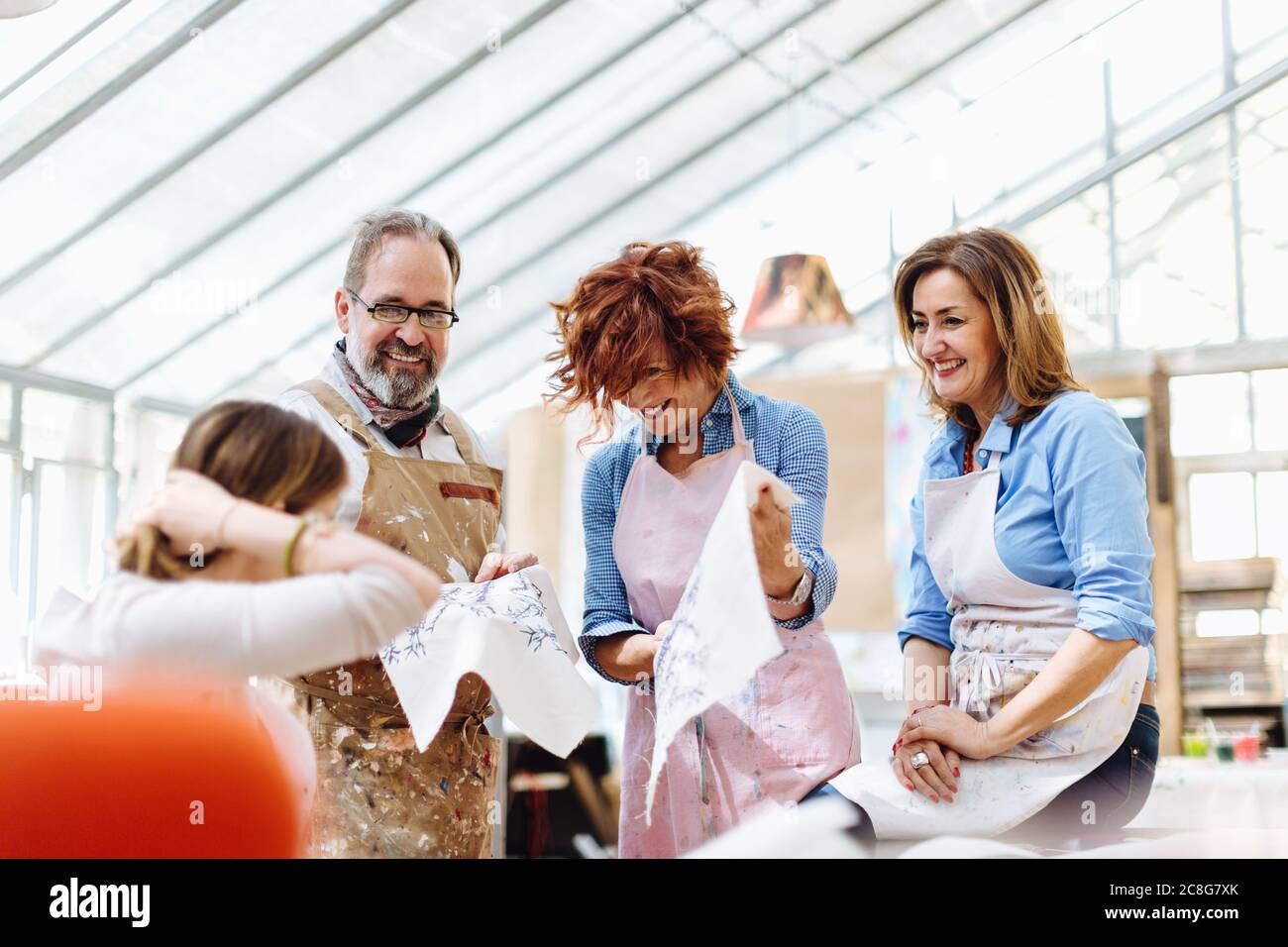 Group of artists looking at painted fabric in creative studio, smiling ...