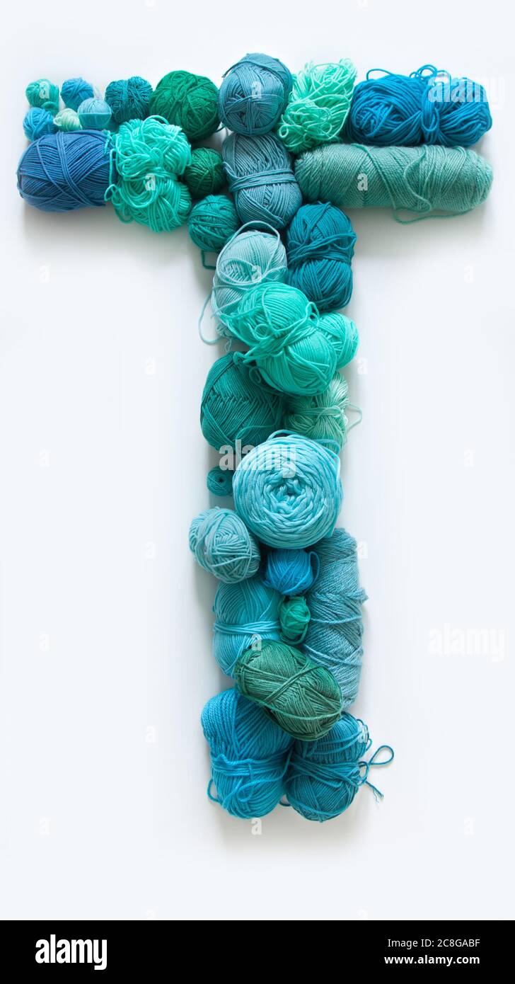 The letter T is made of multi-colored skeins and a ball of yarn. White ...