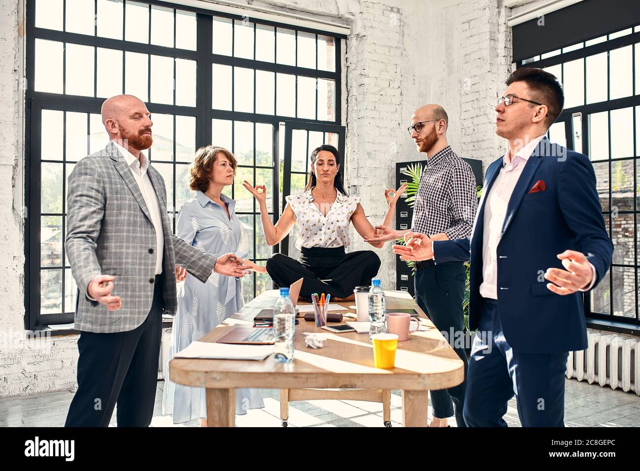 group of young people meditating in office at desk, group meditation ...
