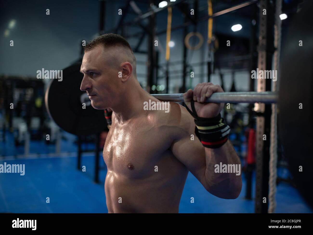 Sweaty athlete doing back squat exercise with barbell on shoulders in ...