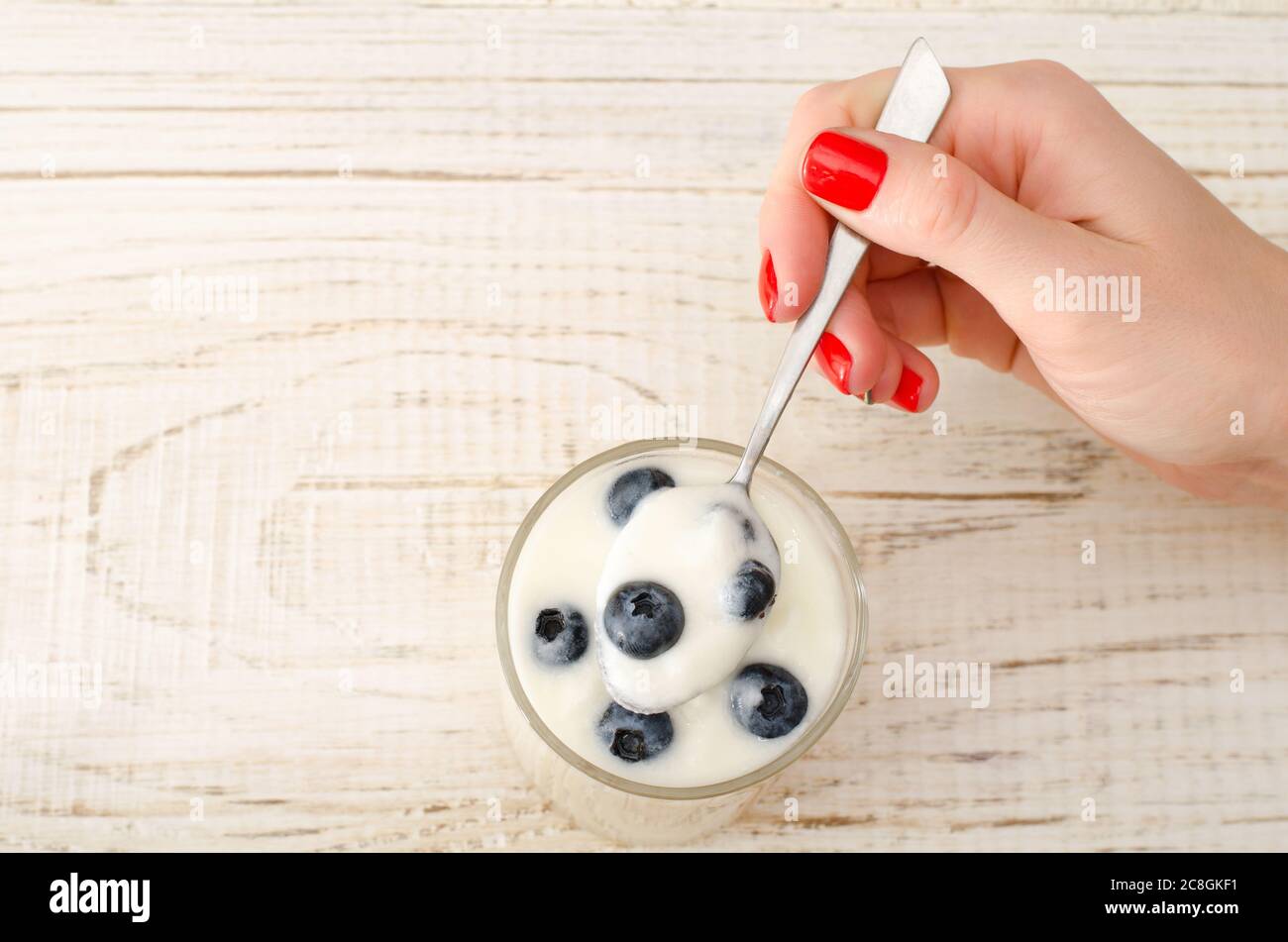 Female hand holding a spoon of yogurt with berries blueberry, light ...