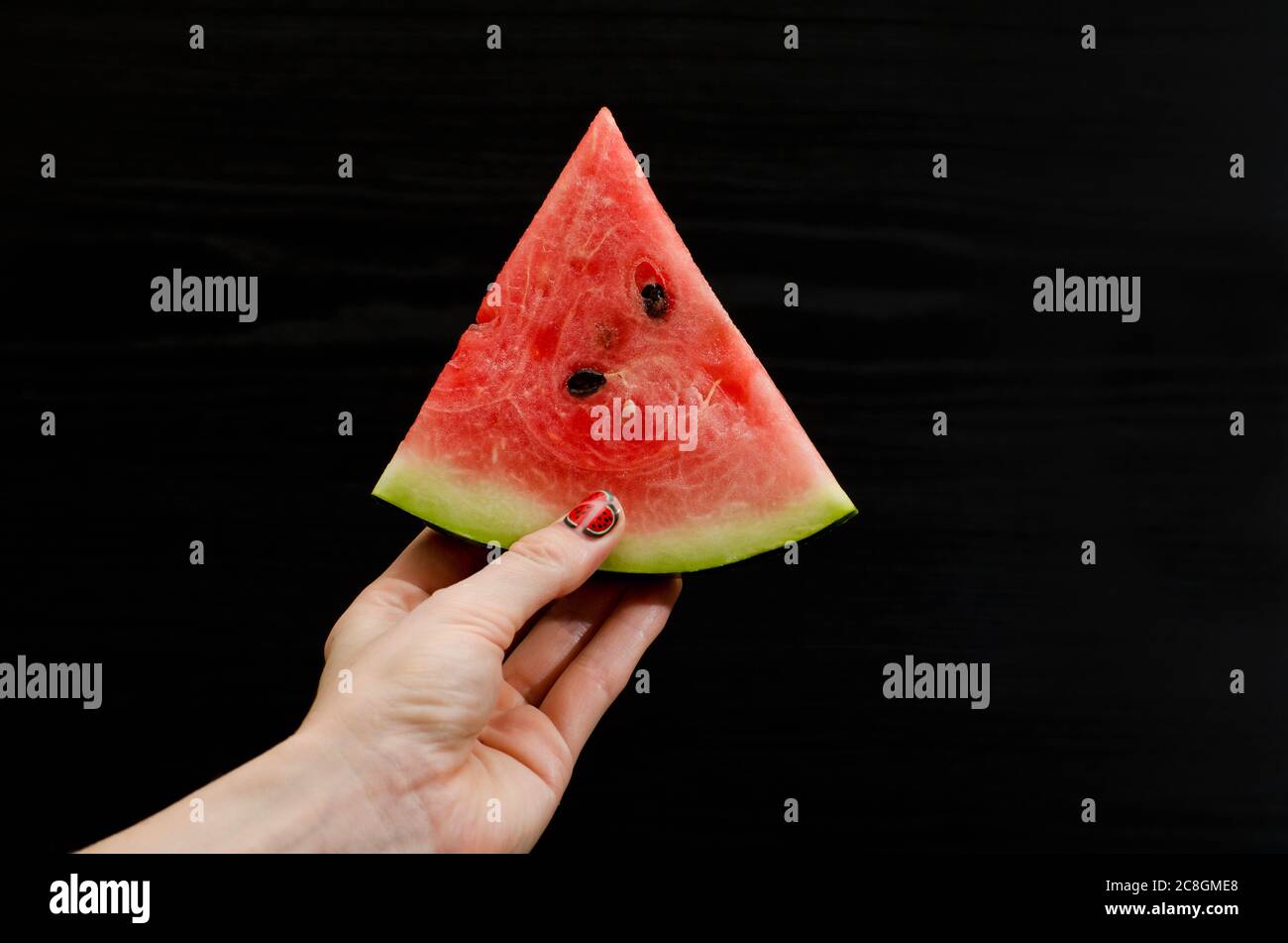 The triangle of watermelon in a female hand on a black background Stock ...