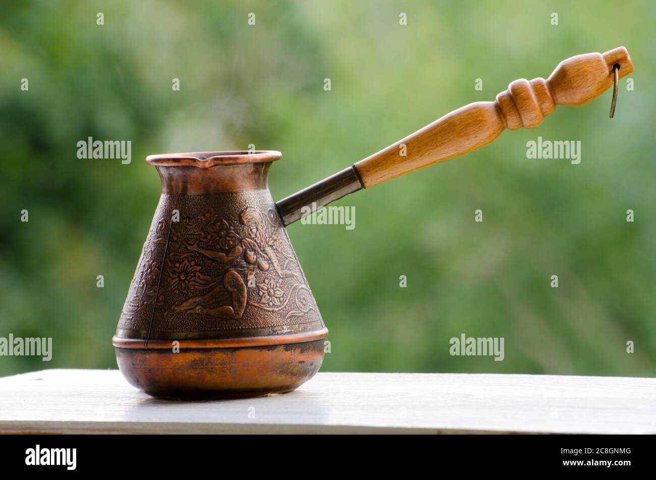 Copper Cezve with hot coffee on a windowsill, blurred green background ...