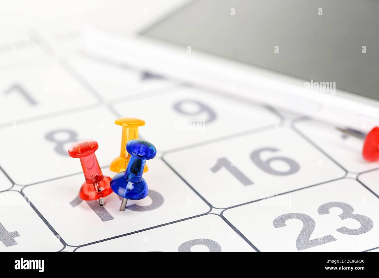 three colorful pushpins pinned on calendar, phone in the background ...