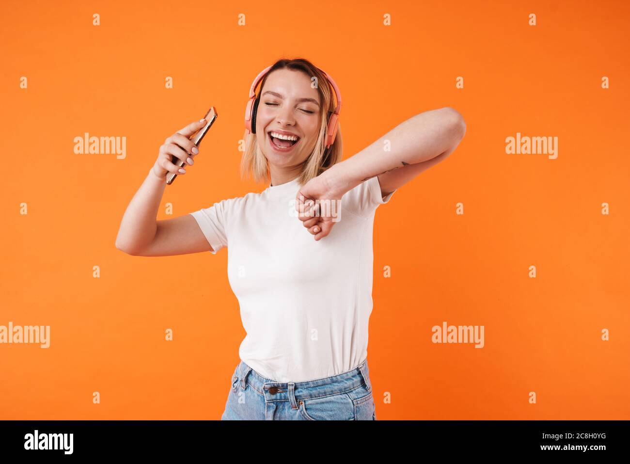 Image of excited young woman dancing using cellphone and headphones ...
