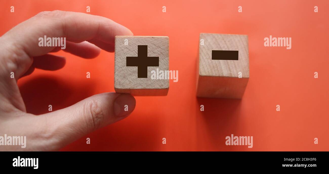 Wooden block in hand on red with plus and minus signs. Decision making ...