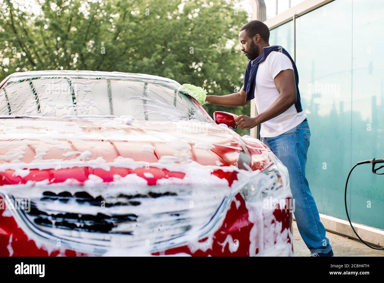 Outdoor car wash concept. Portrait of young African man washing his car ...