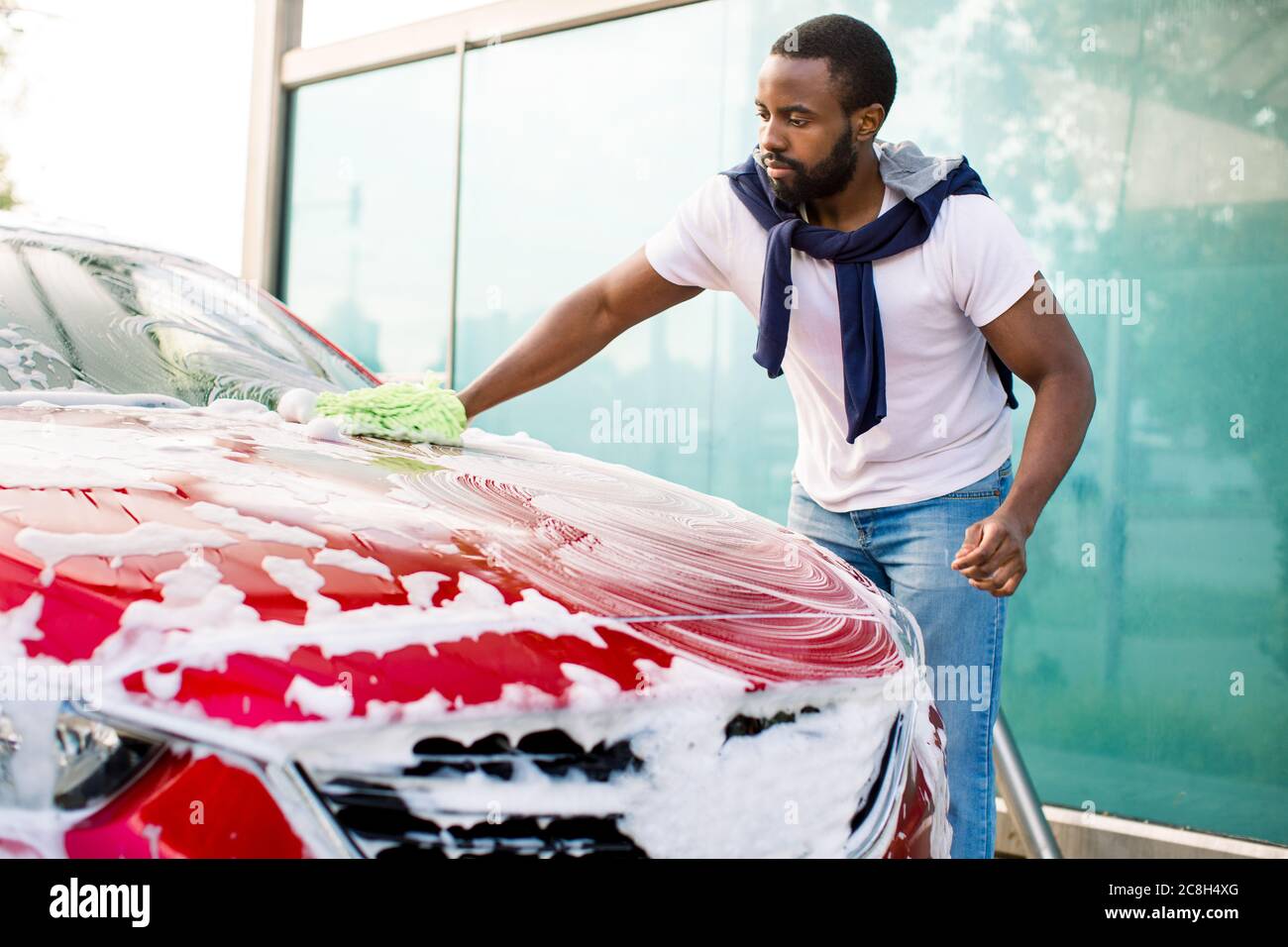Side angle view of young handsome African man washing his red car hood ...