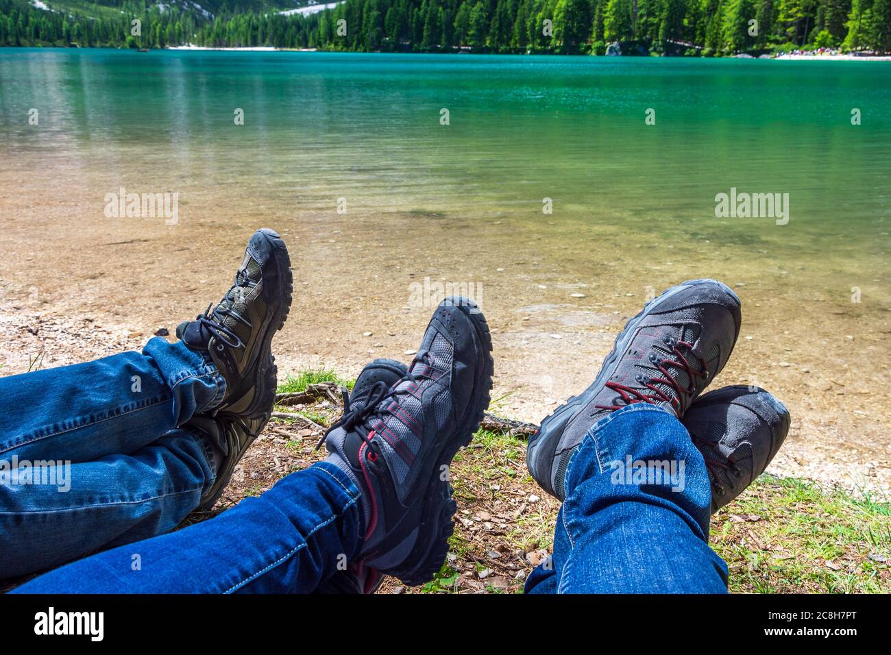 Trekking legs of friends who are on the shore of a lake and enjoy the ...