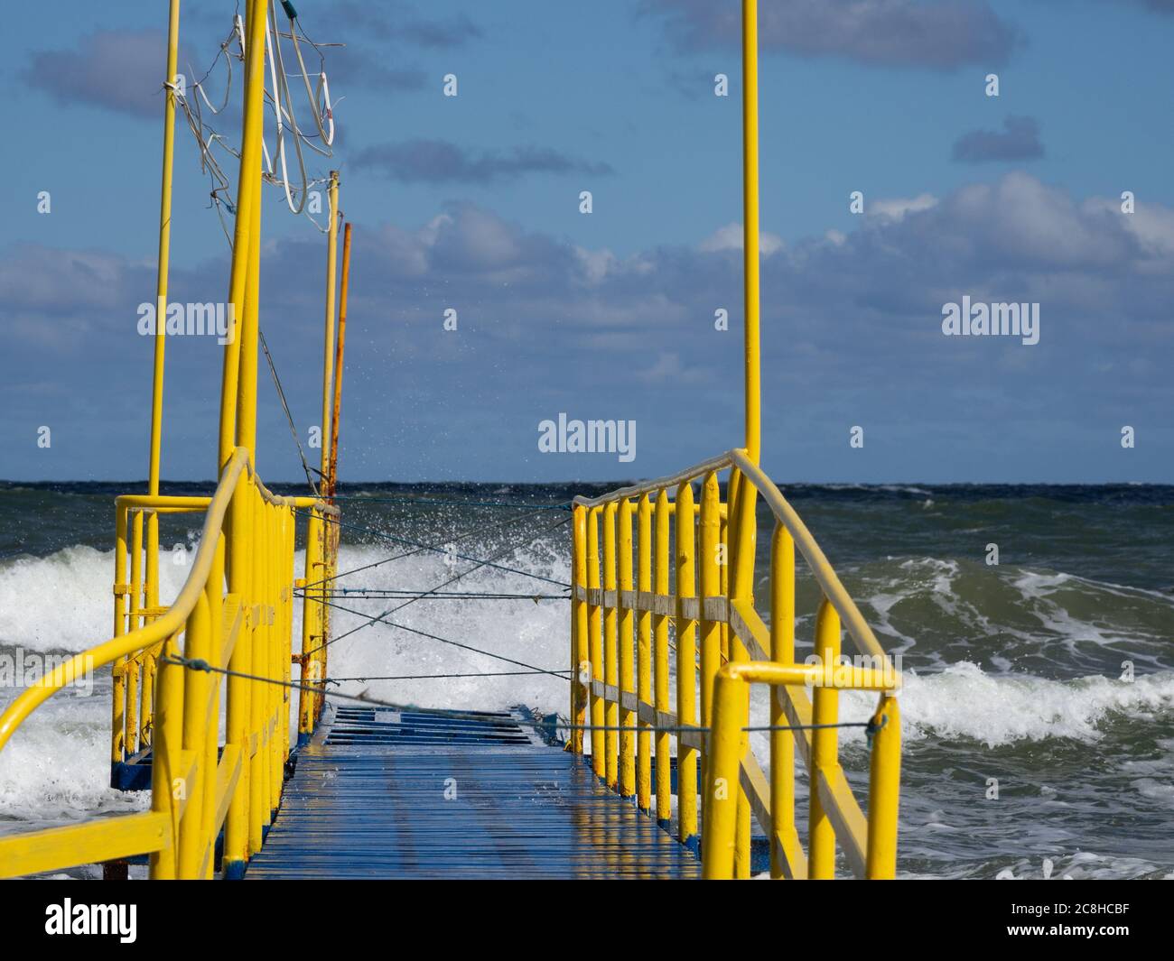 a blue wooden footbridge with yellow railings leads into the Baltic Sea ...