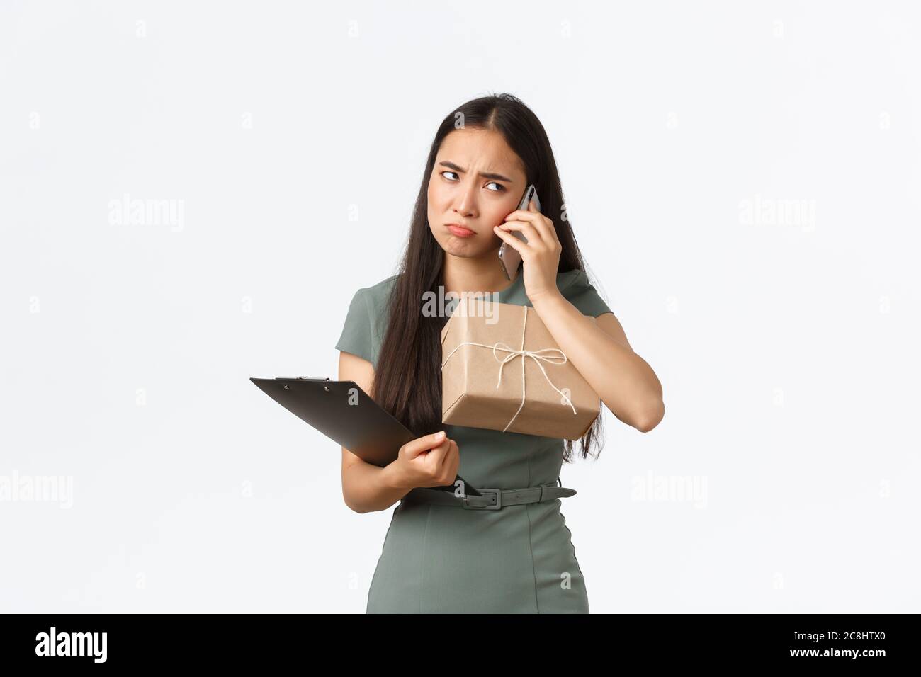 Upset pouting asian businesswoman holding clients package and clipboard ...