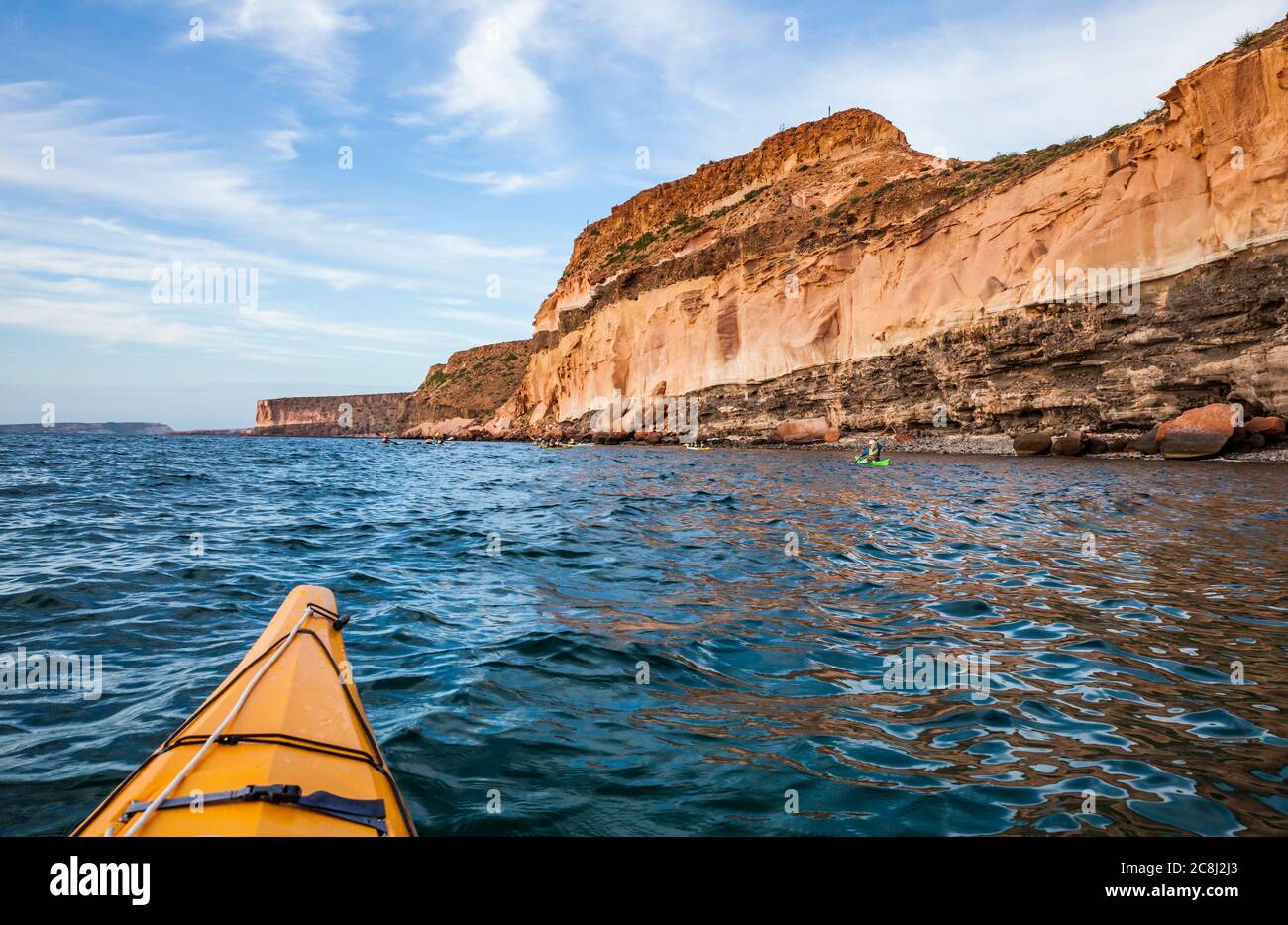 A guided sea kayaking tour offshore below towering sandstone cliffs on ...
