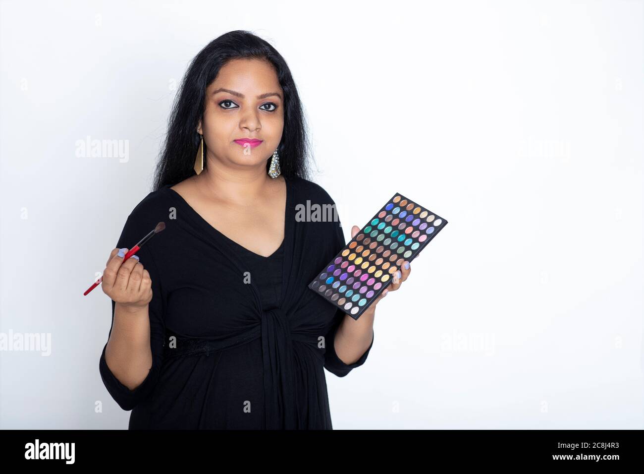 Young attractive Indian female using eye shadow brush and holding ...