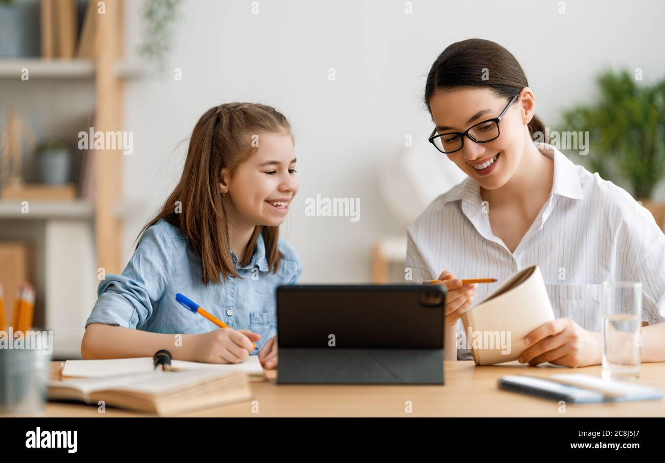 Back to school. Happy child and adult are sitting at desk. Girl doing ...