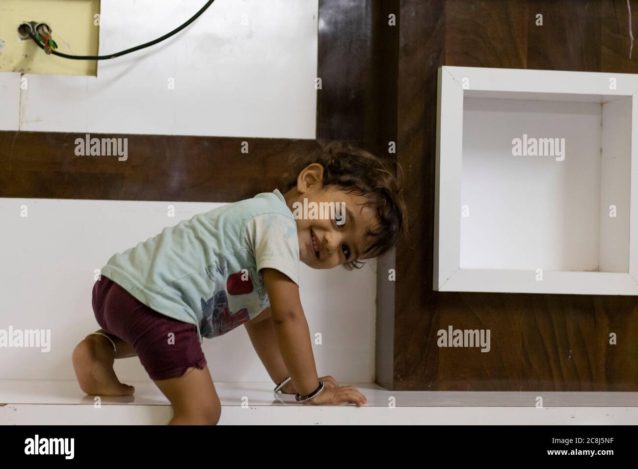 A small child climbing on a small wooden table looking back And showing ...